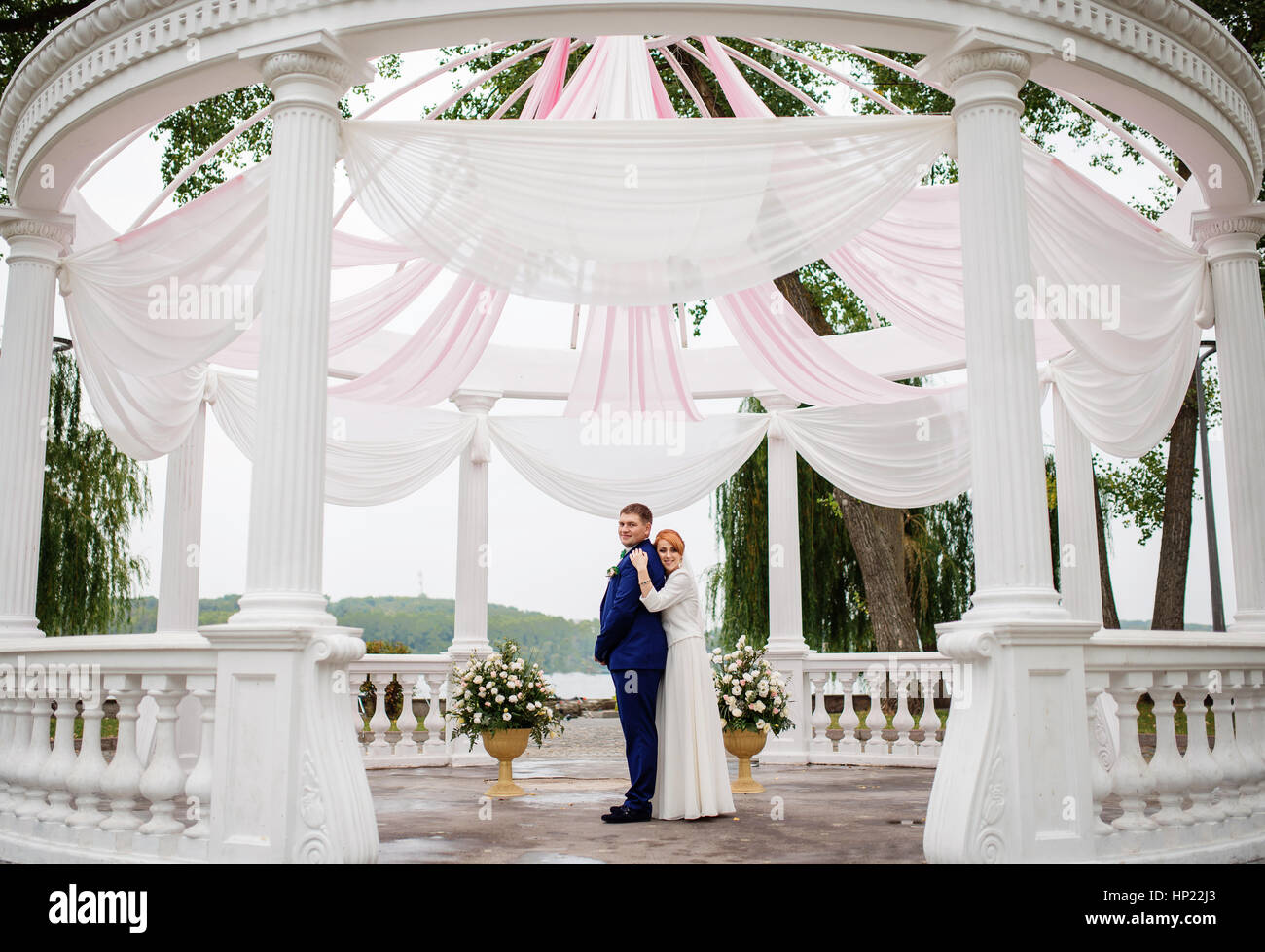Wedding couple under large arch with pink material decoration with ...