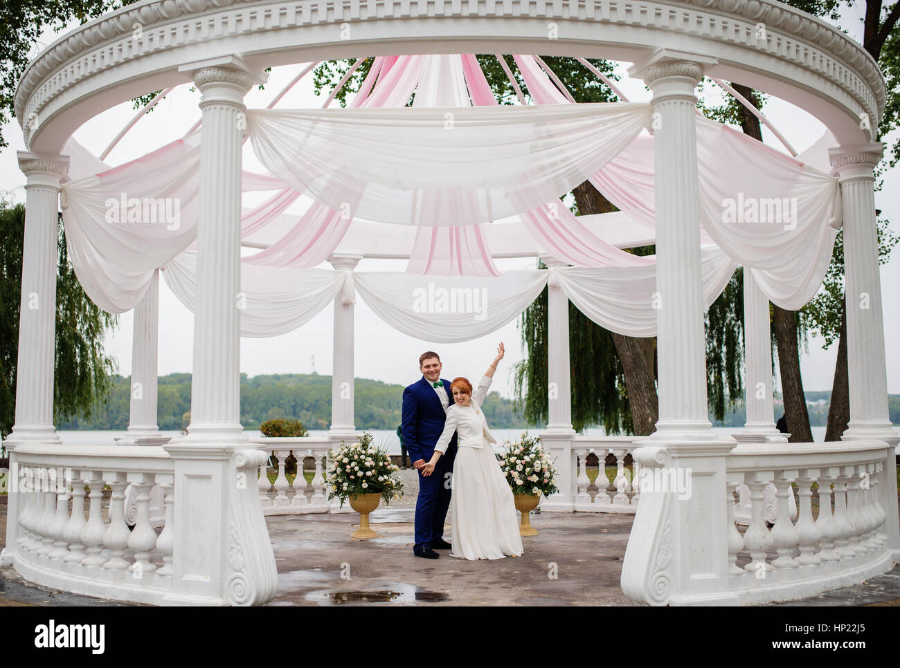 Wedding couple under large arch with pink material decoration with ...
