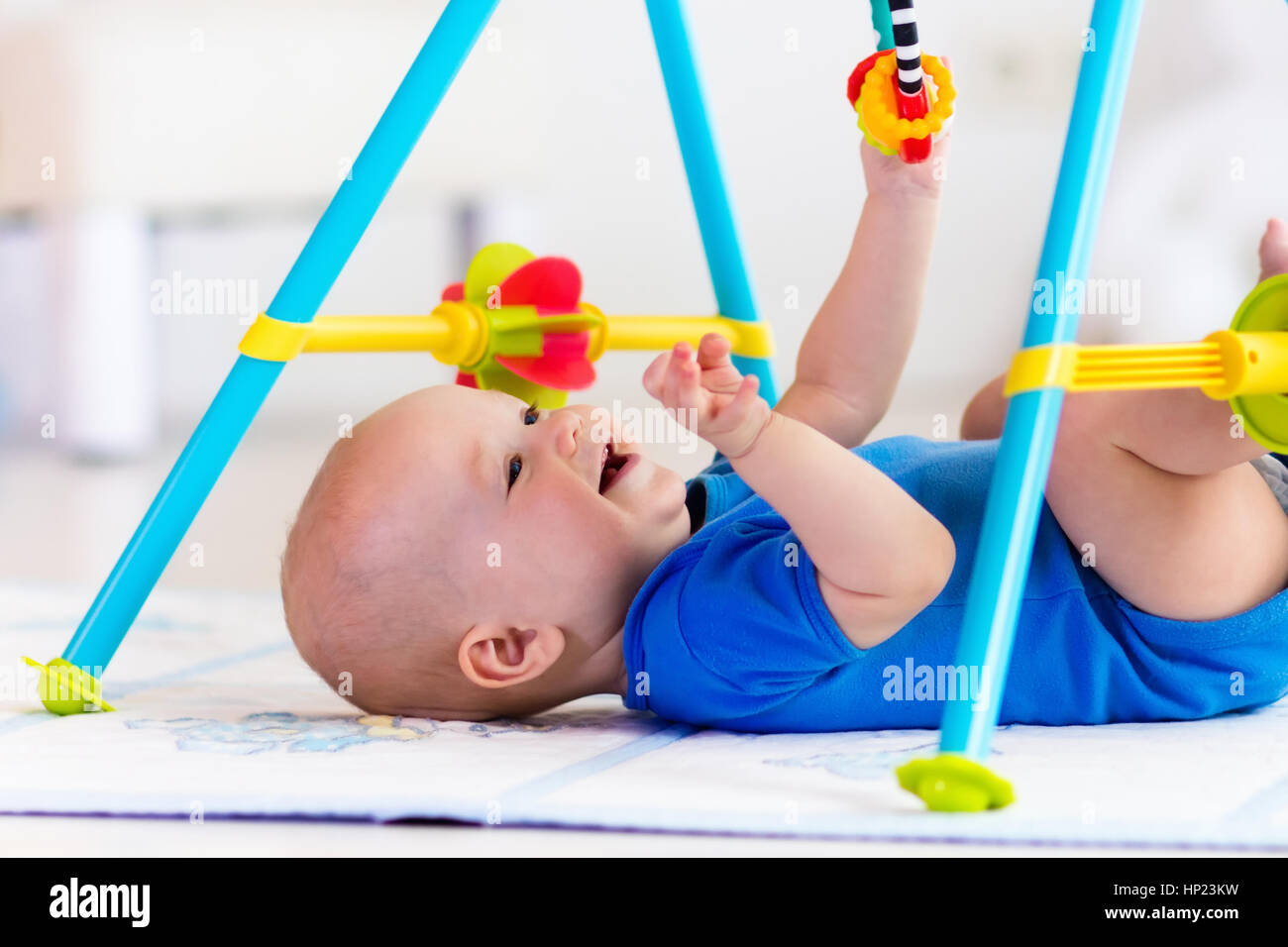 Cute baby boy on colorful playmat and gym, playing with hanging rattle ...