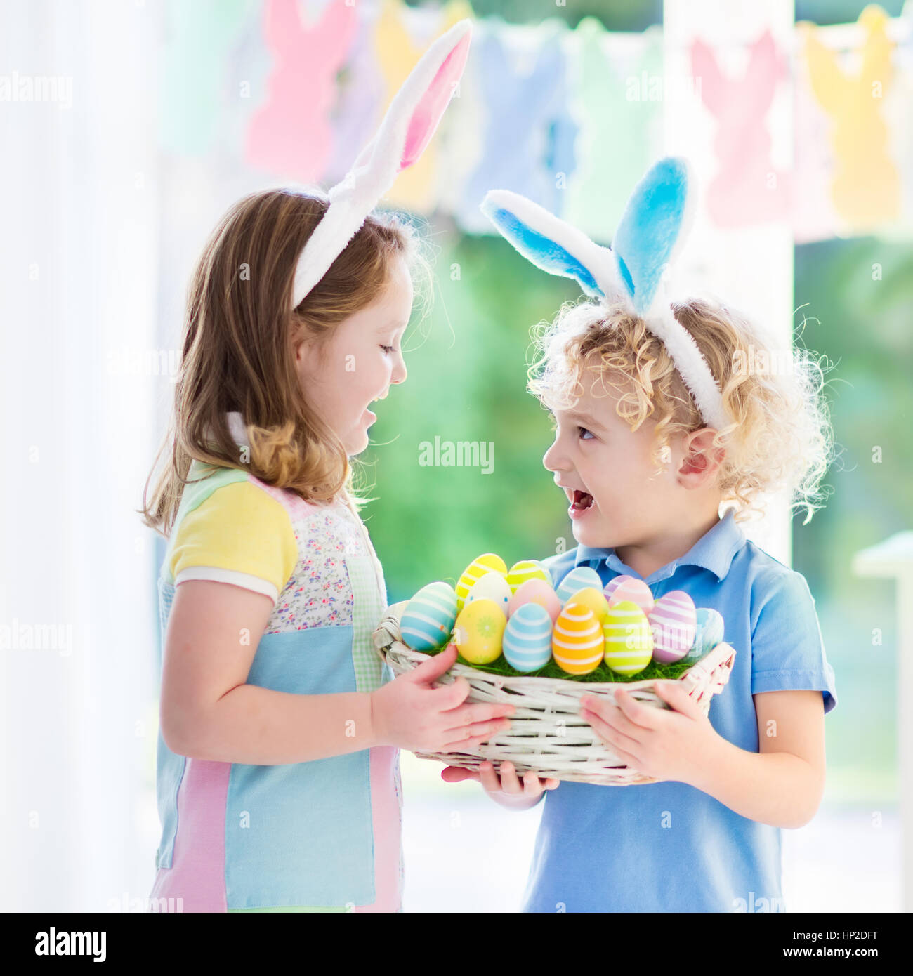 Little boy and girl in bunny ears holding a basket with colorful Easter ...