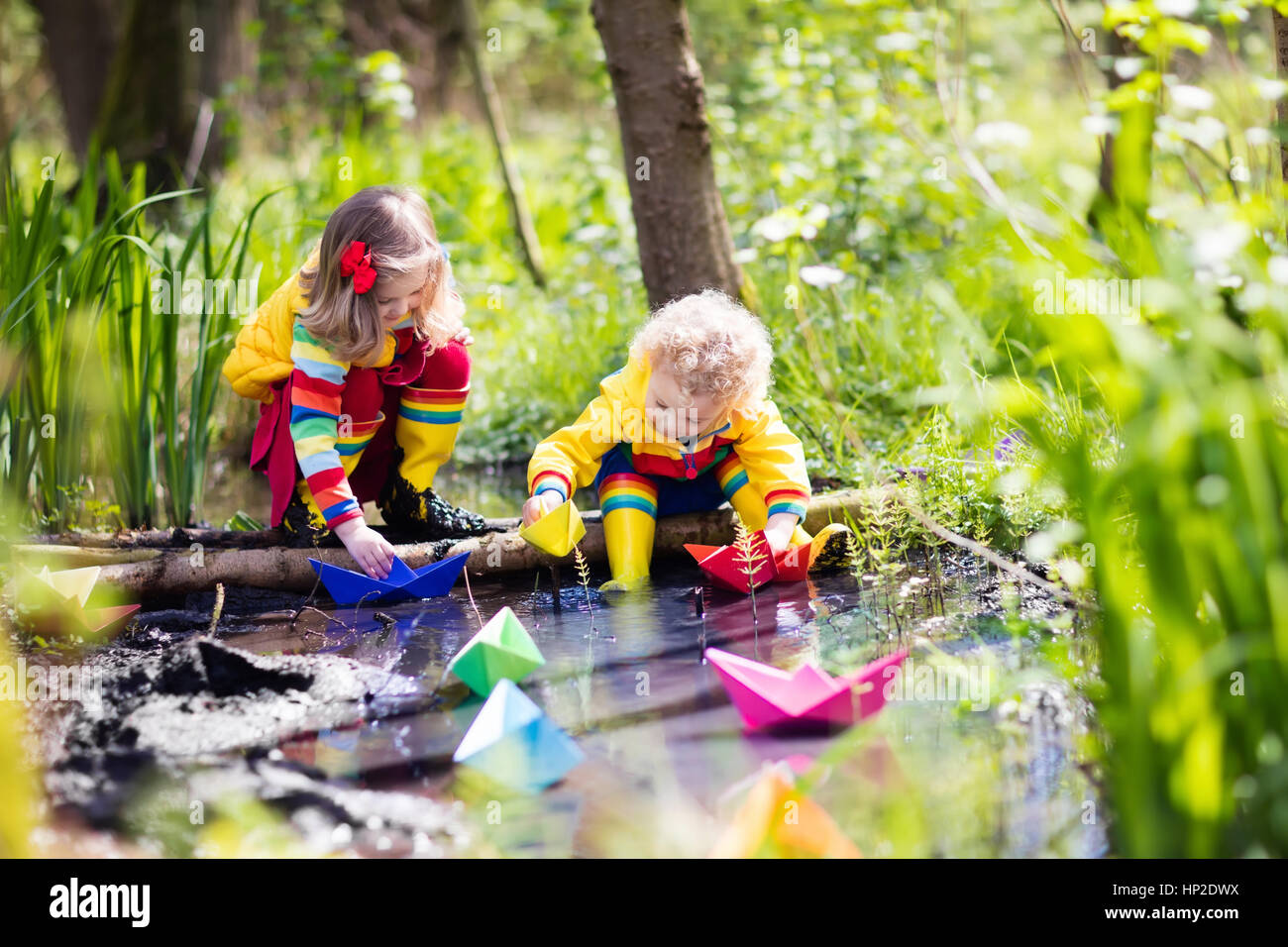 Children play with colorful paper boats in a small river on a sunny ...