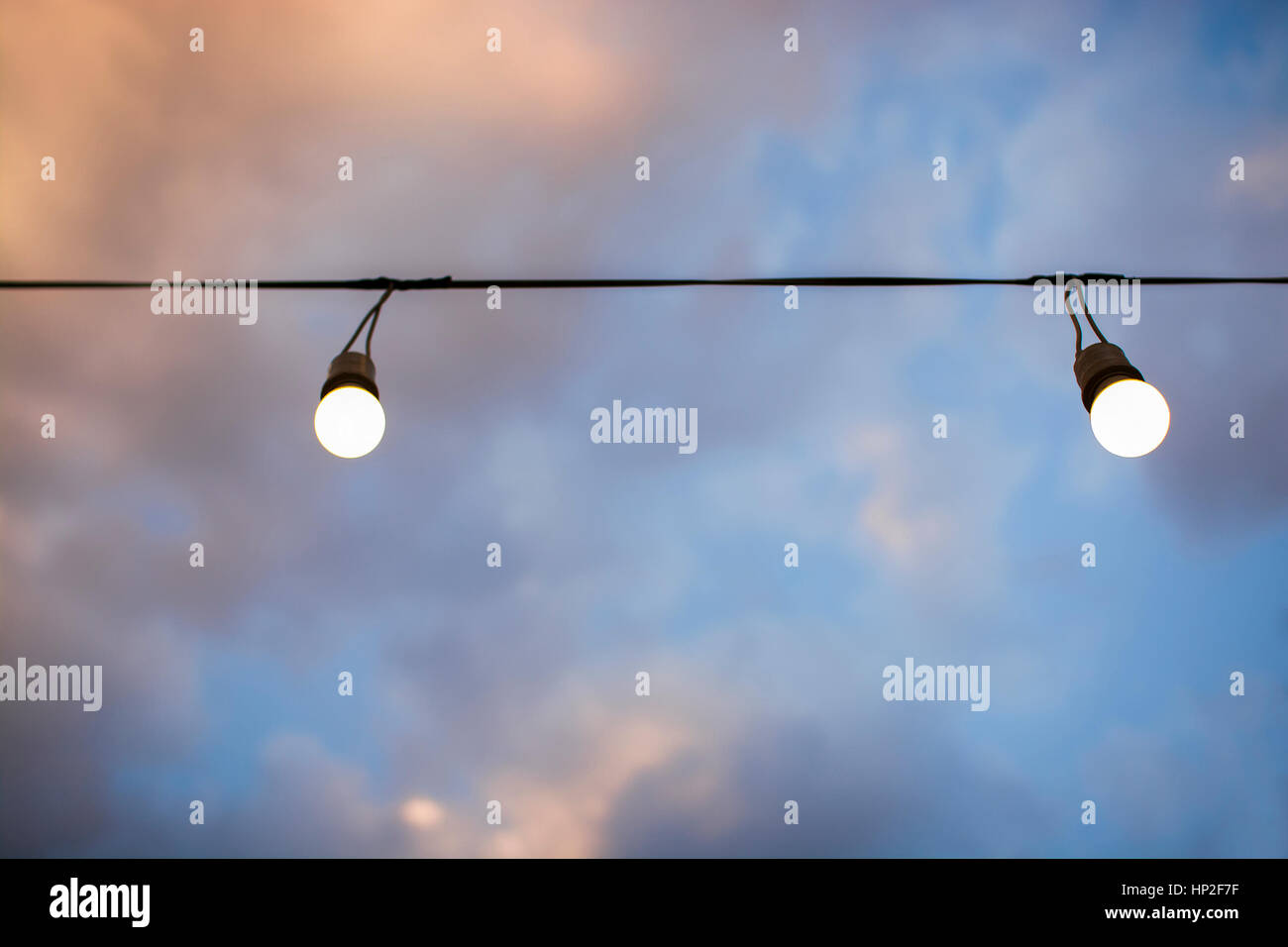 Electric lamps with light hanging on electric wire and sky background ...