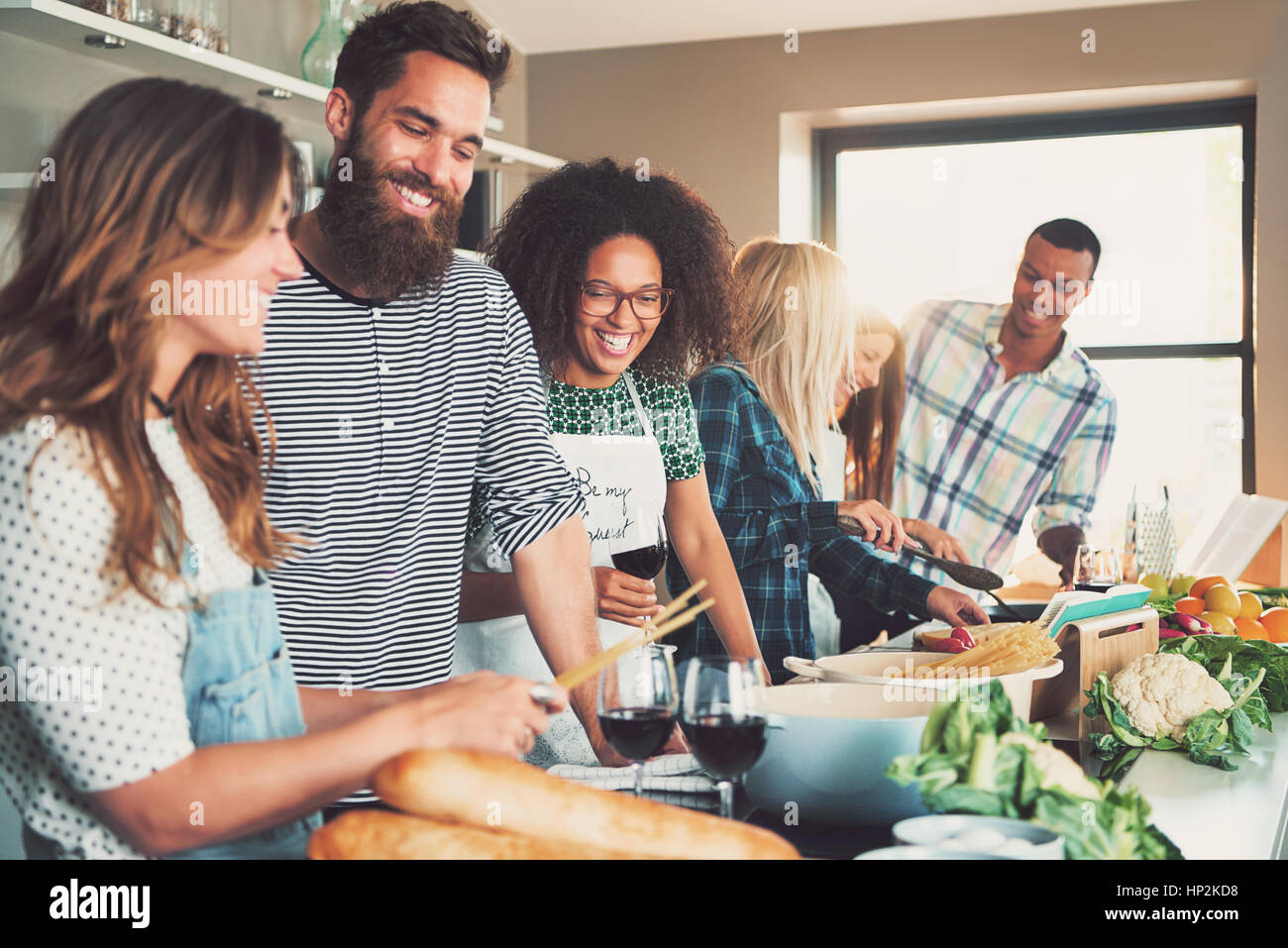 Group of young smiling cheerful friends cooking some meal at kitchen ...