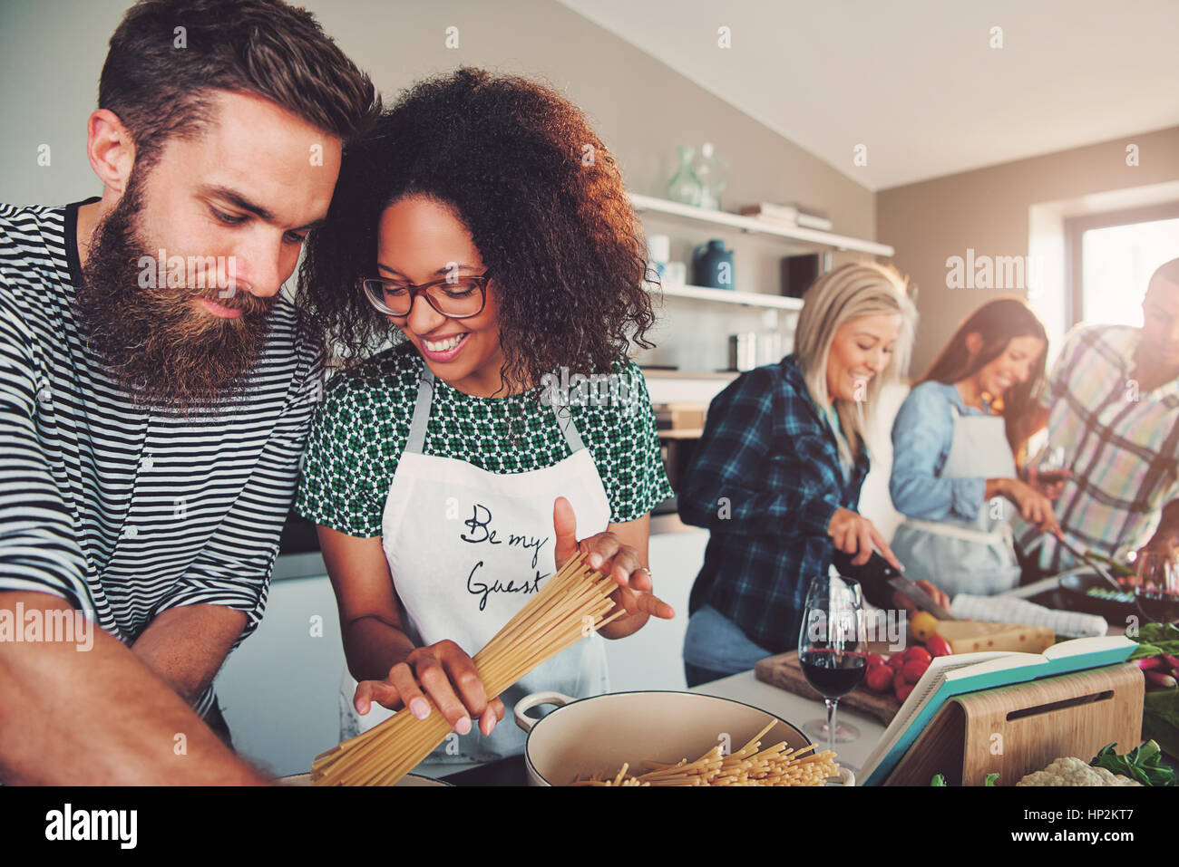 Mixed group of good friends preparing pasta dinner in kitchen together ...