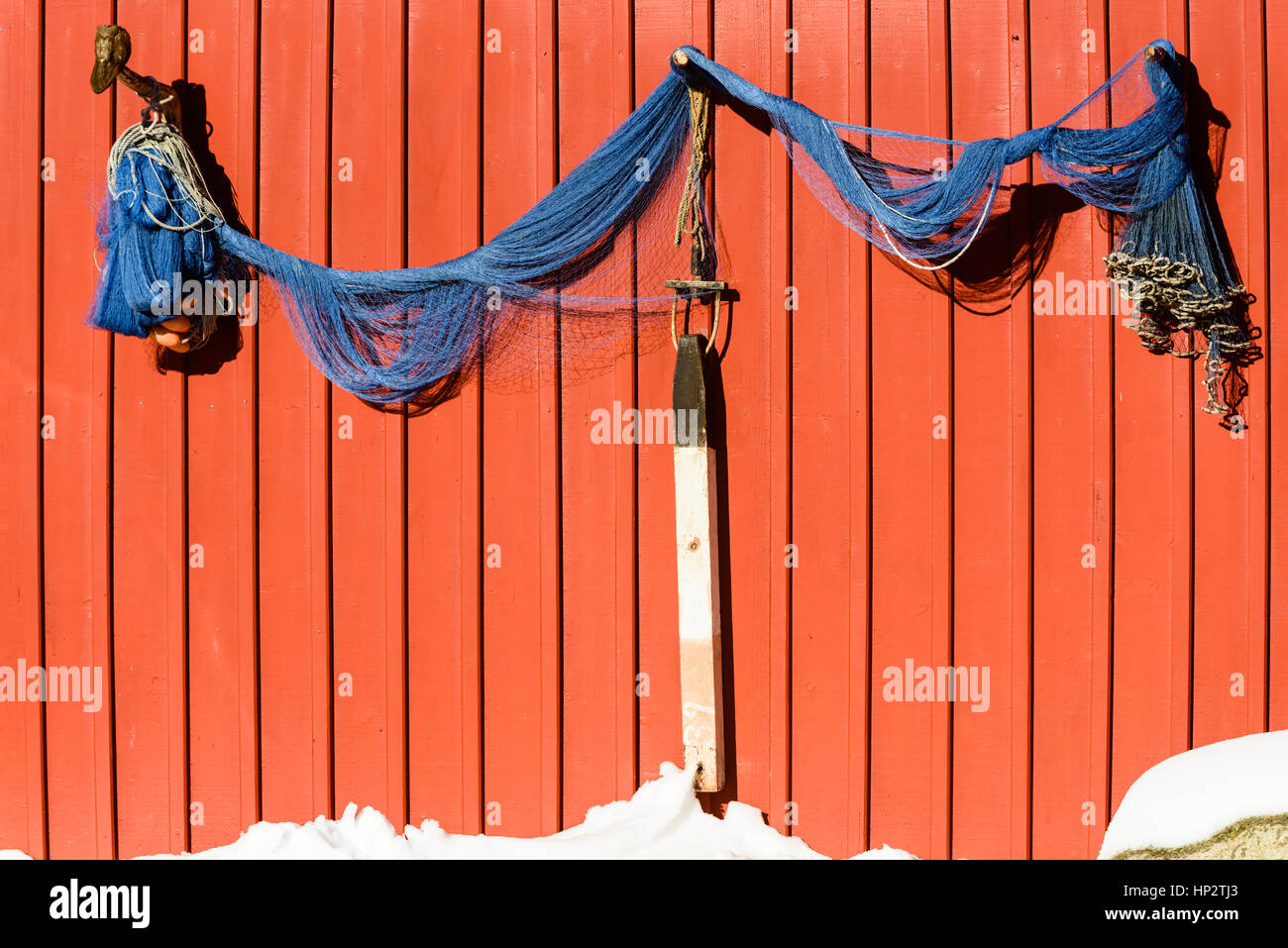Blue fishing net hanging on the red wooden wall of a shed. Some snow ...