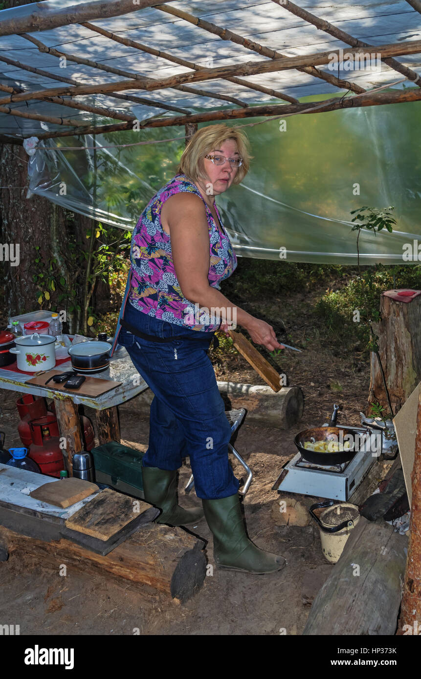 Forest camping kitchen.The woman, gas and a frying pan in the wood ...