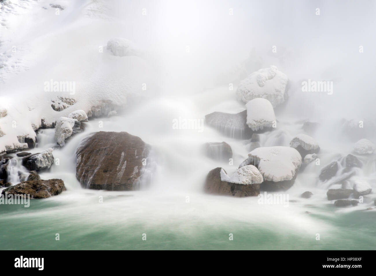 Snow covered rocks under water and mist from waterfall flowing into ...