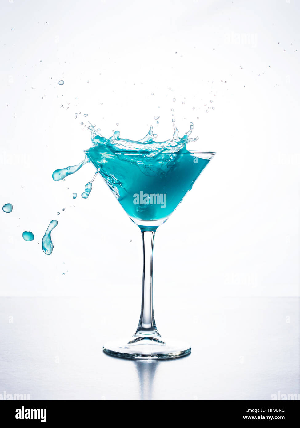 Blue cocktail in martini glass with ice cube splashing into liquid ...