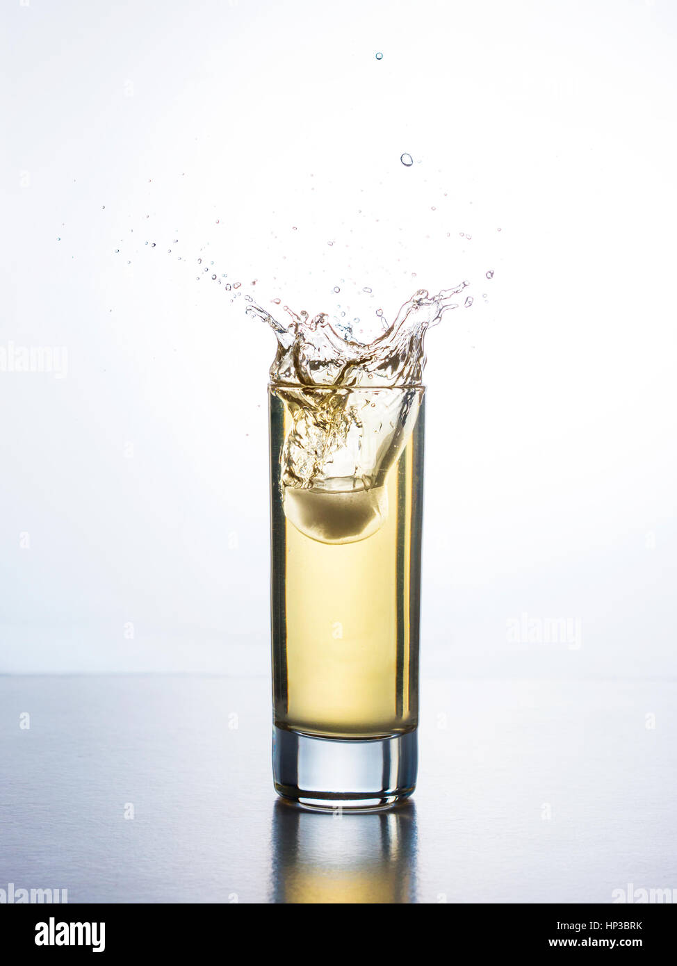 Yellow apple juice in glass with ice cube splashing into liquid against ...