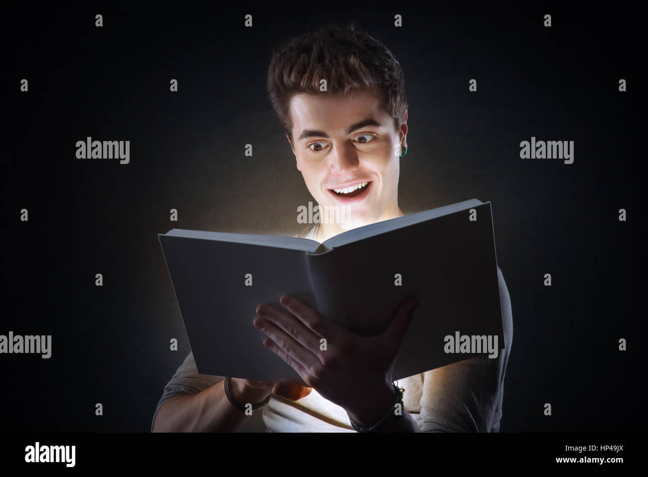Young smiling man reading an exciting book glowing in the dark Stock ...