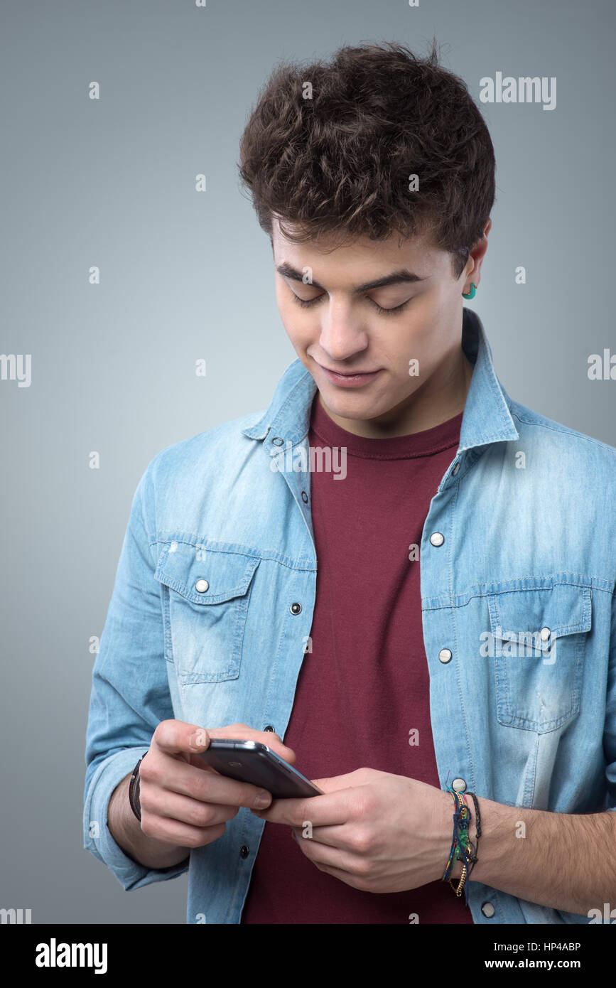Smiling teenager boy texting and using a touch screen mobile phone ...