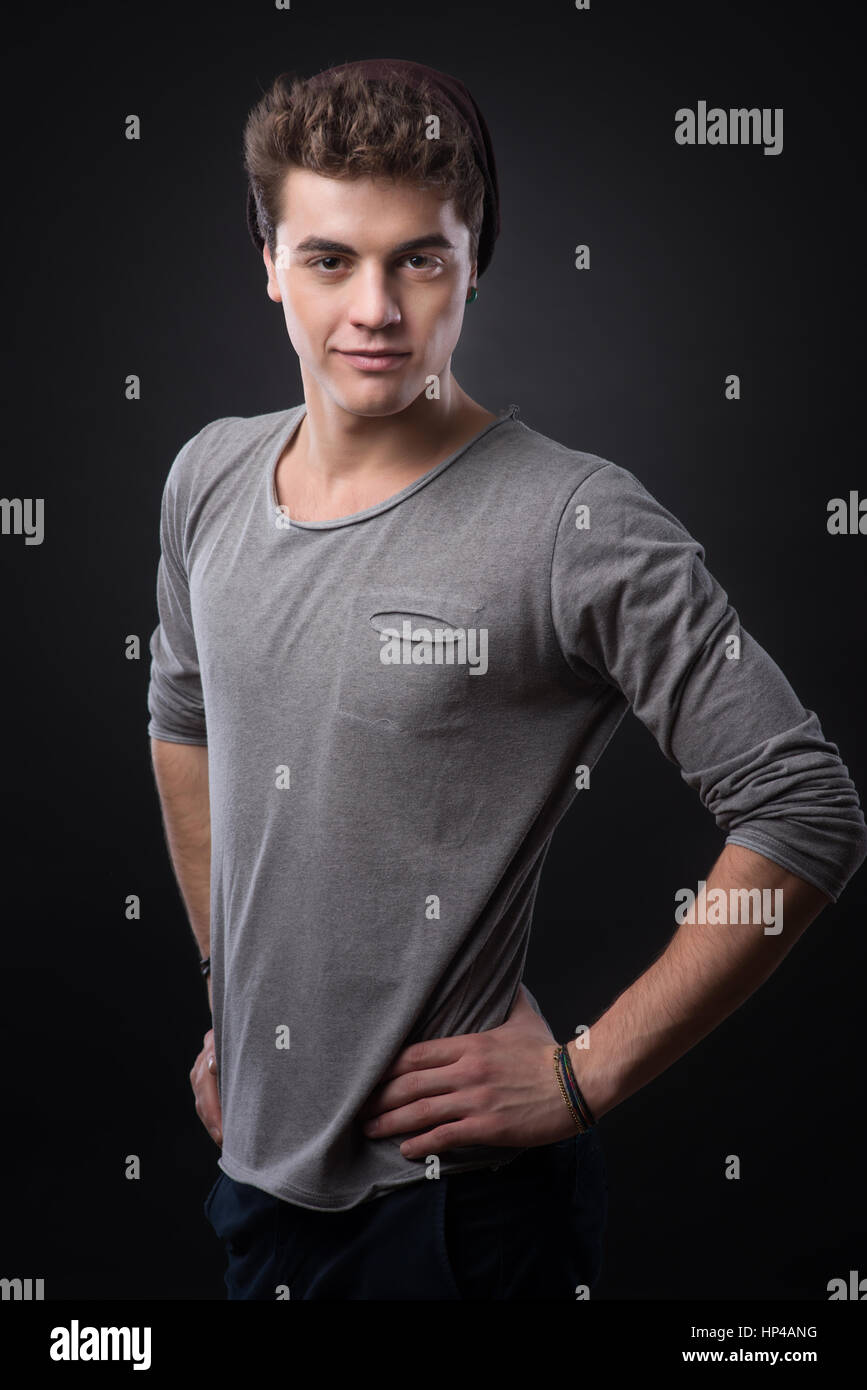 Confident young man posing in assertive position and smiling at camera ...