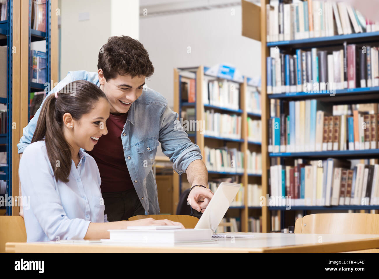 Schoolmates studying together at the library with bookshelves on ...