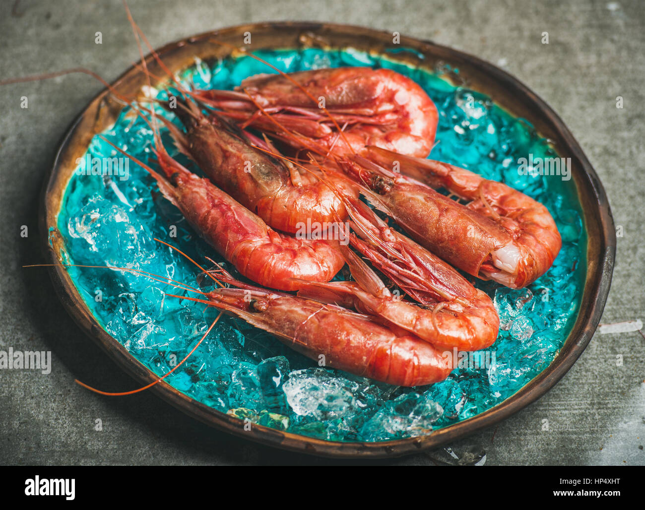 Raw uncooked red shrimps on chipped ice in turquoise blue ceramic tray ...