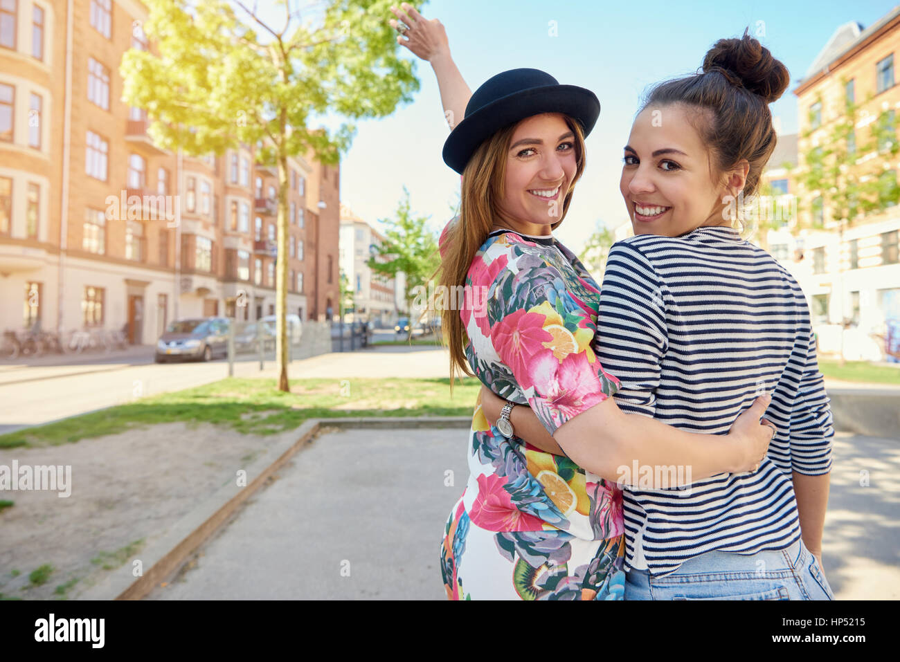 Happy friendly trendy young women walking arm in arm along a quiet ...