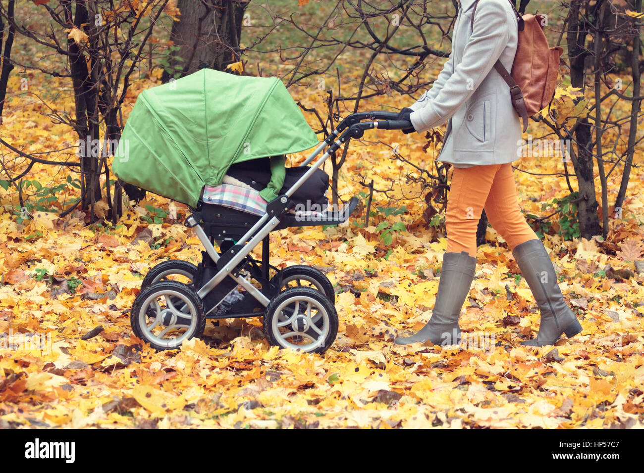Mother pushing stroller in autumn park. Young woman strolling with a ...