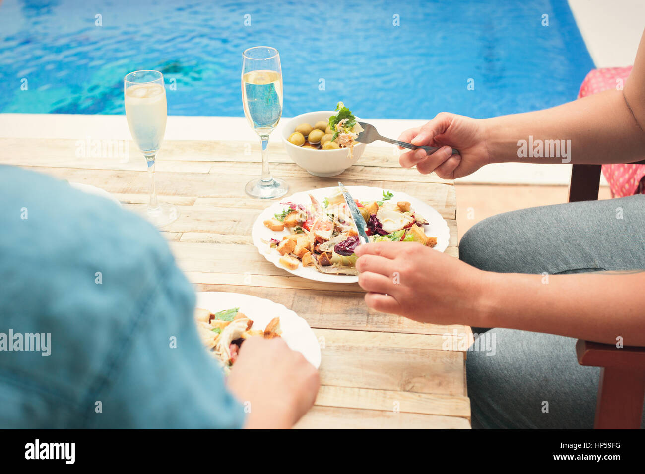 Young people sitting by the pool having dinner with champagne, salad ...