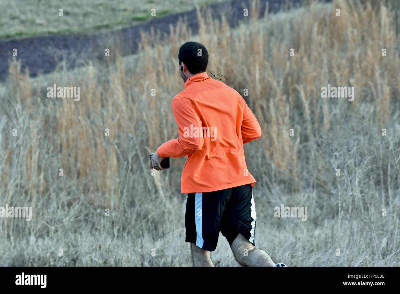 A man with an orange jacket running down an outdoor trail Stock Photo ...