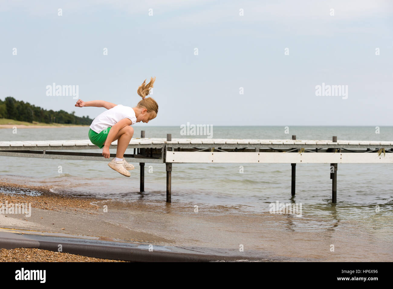 Girl jumping over water at a lakeshore. Copy space in sky if needed ...