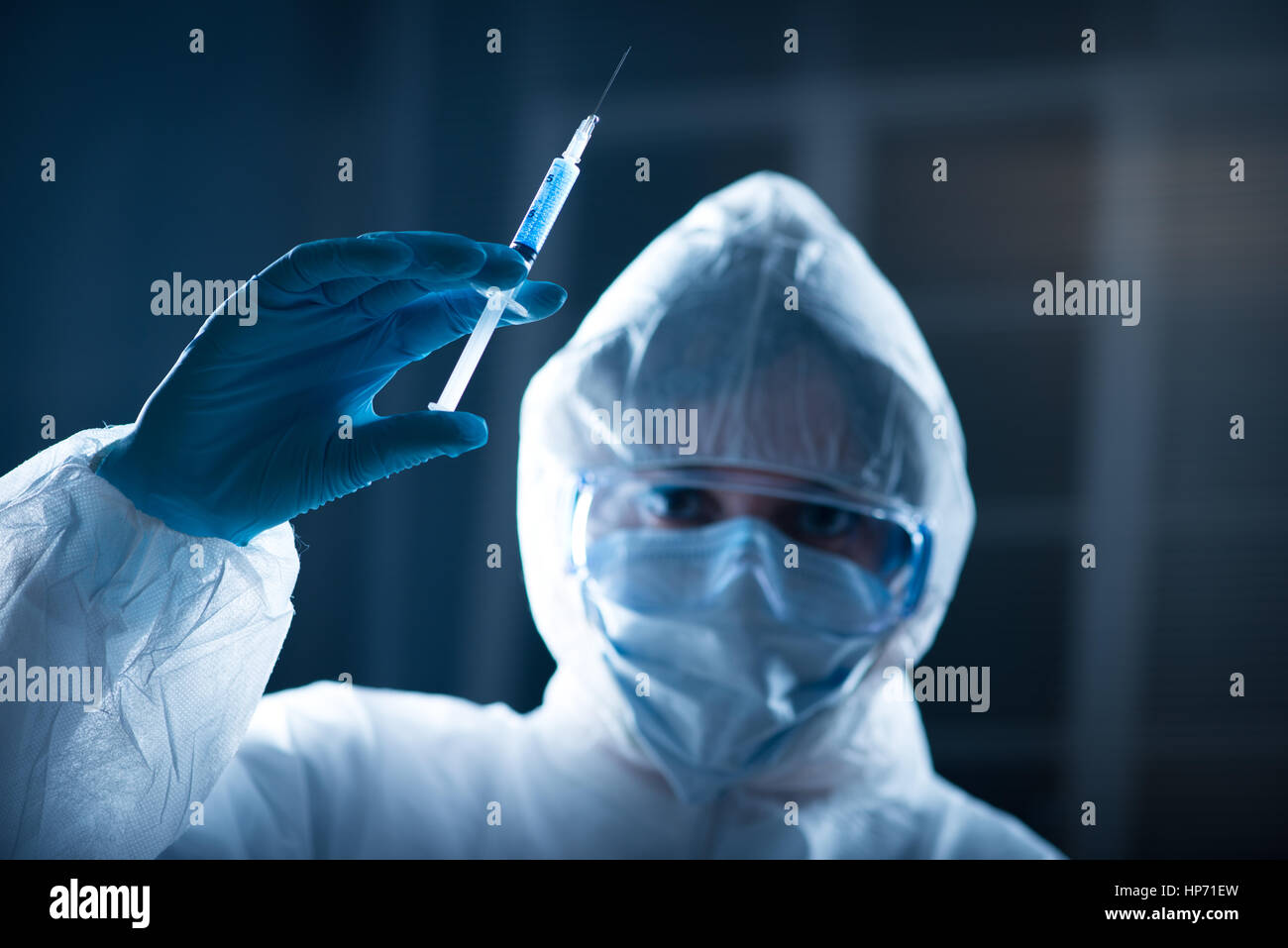 Researcher in hazmat protective suit preparing a syringe for injection ...