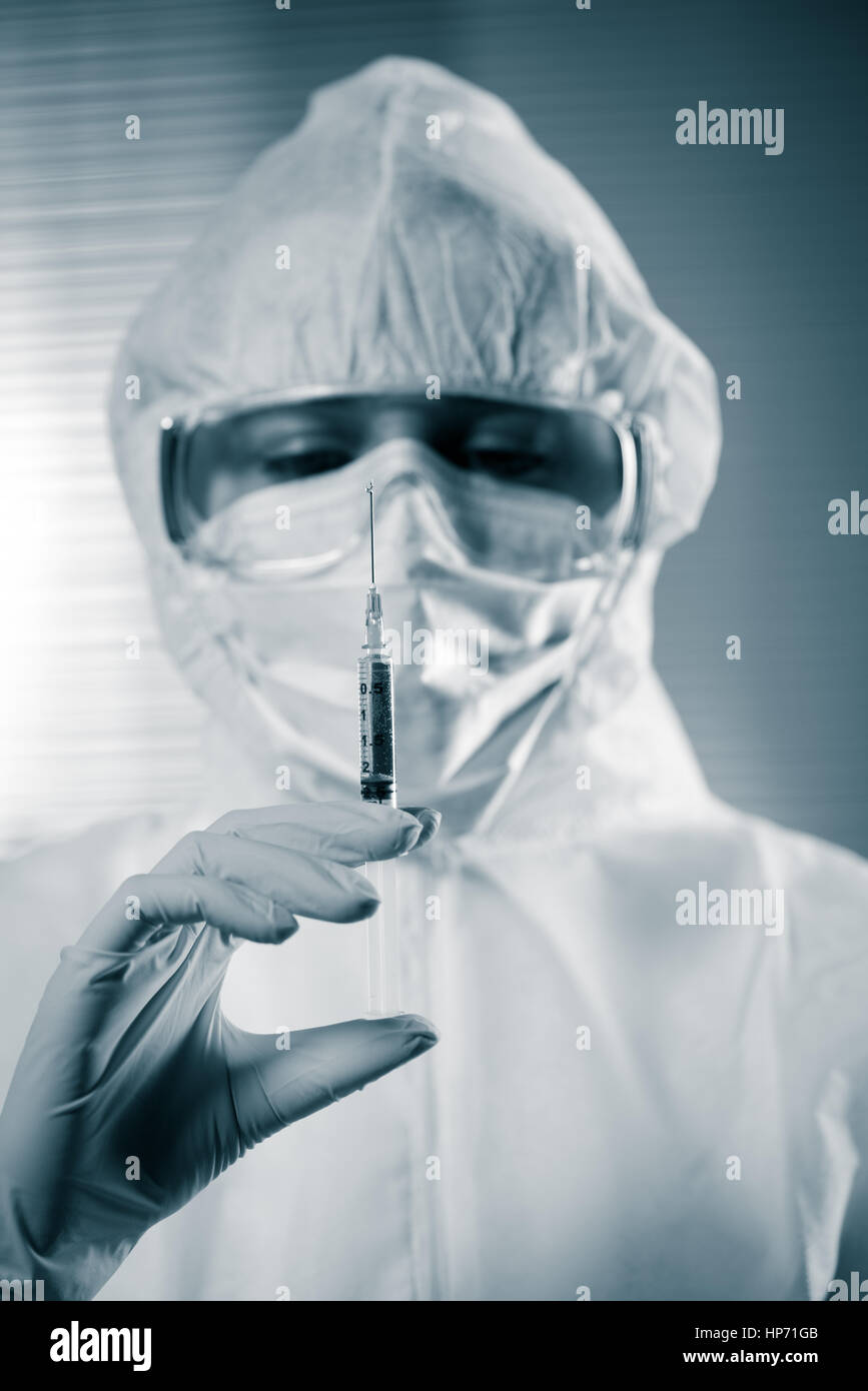 Researcher in hazmat protective suit preparing a syringe for injection ...