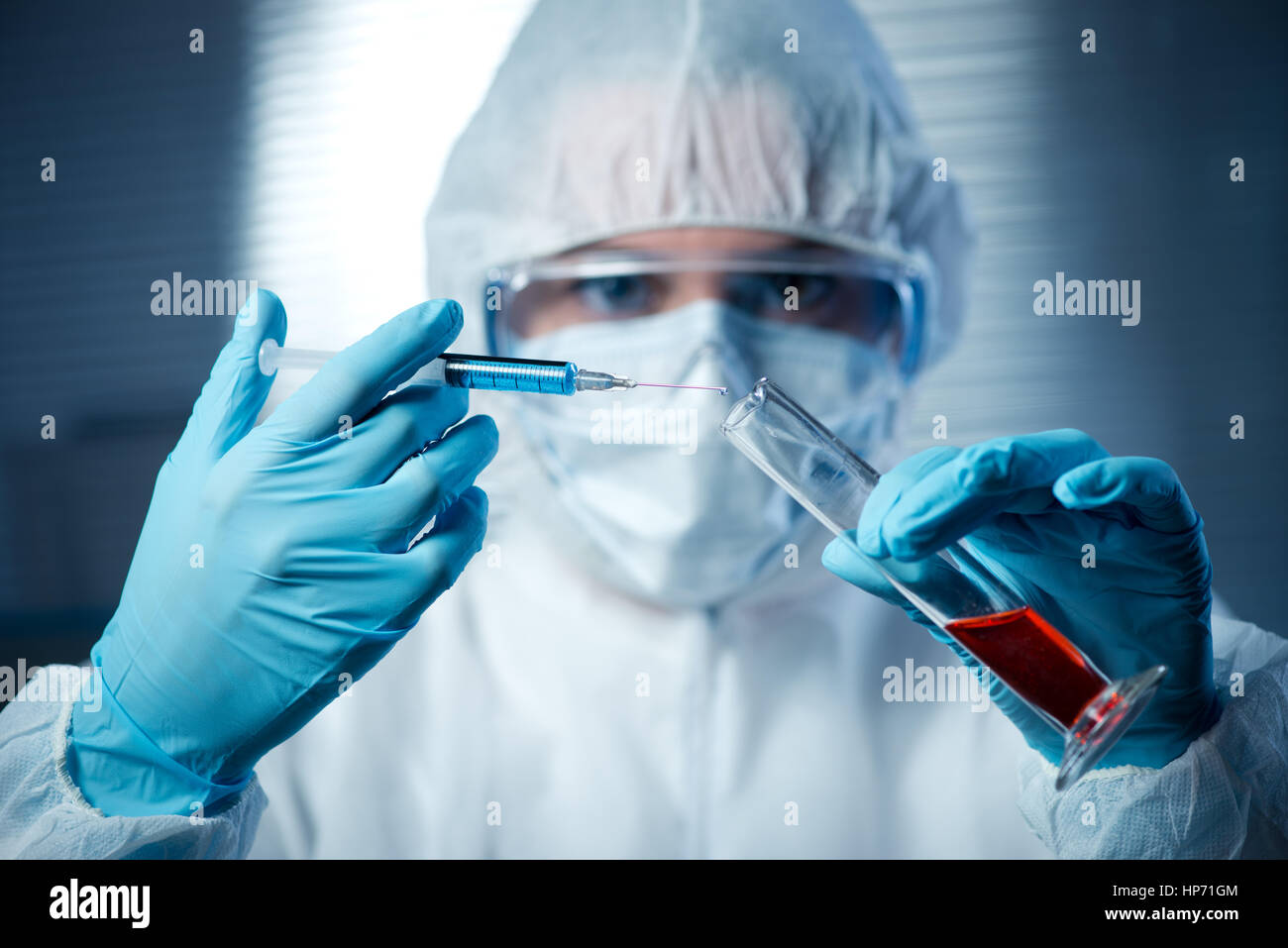 Researcher in safety hazmat suit preparing a syringe for injection with ...