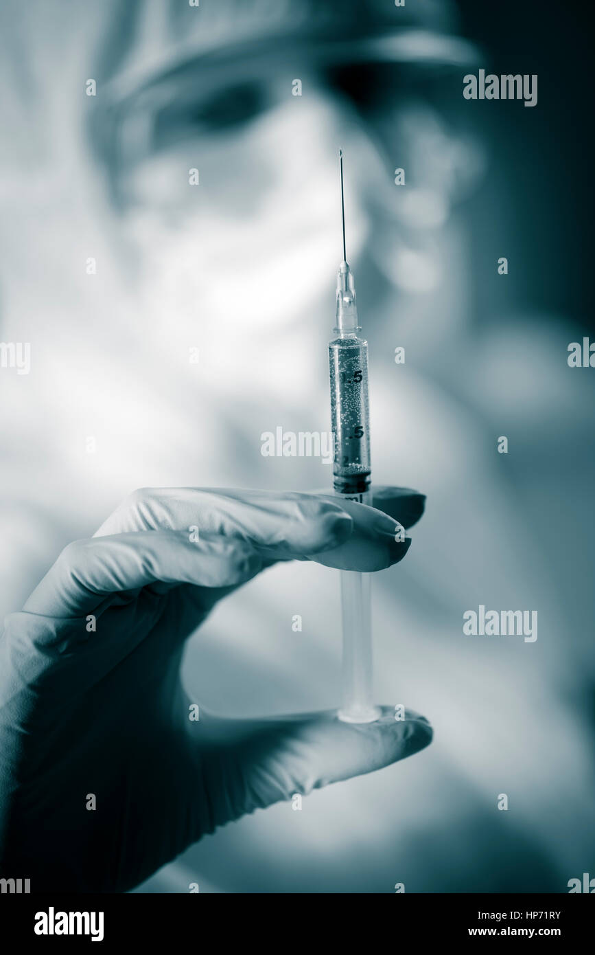 Researcher in hazmat protective suit preparing a syringe for injection ...