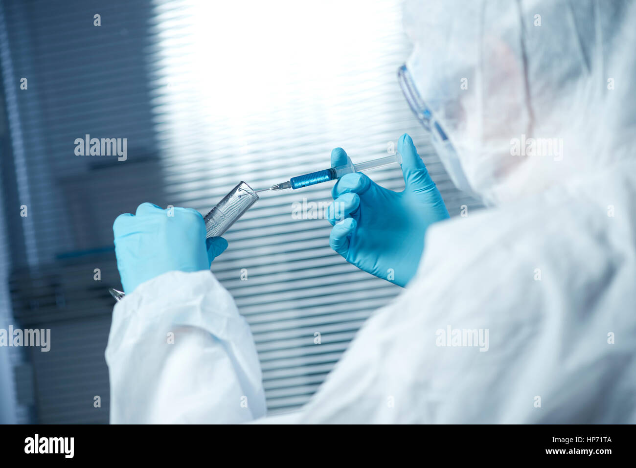 Researcher in safety hazmat suit preparing a syringe for injection with ...