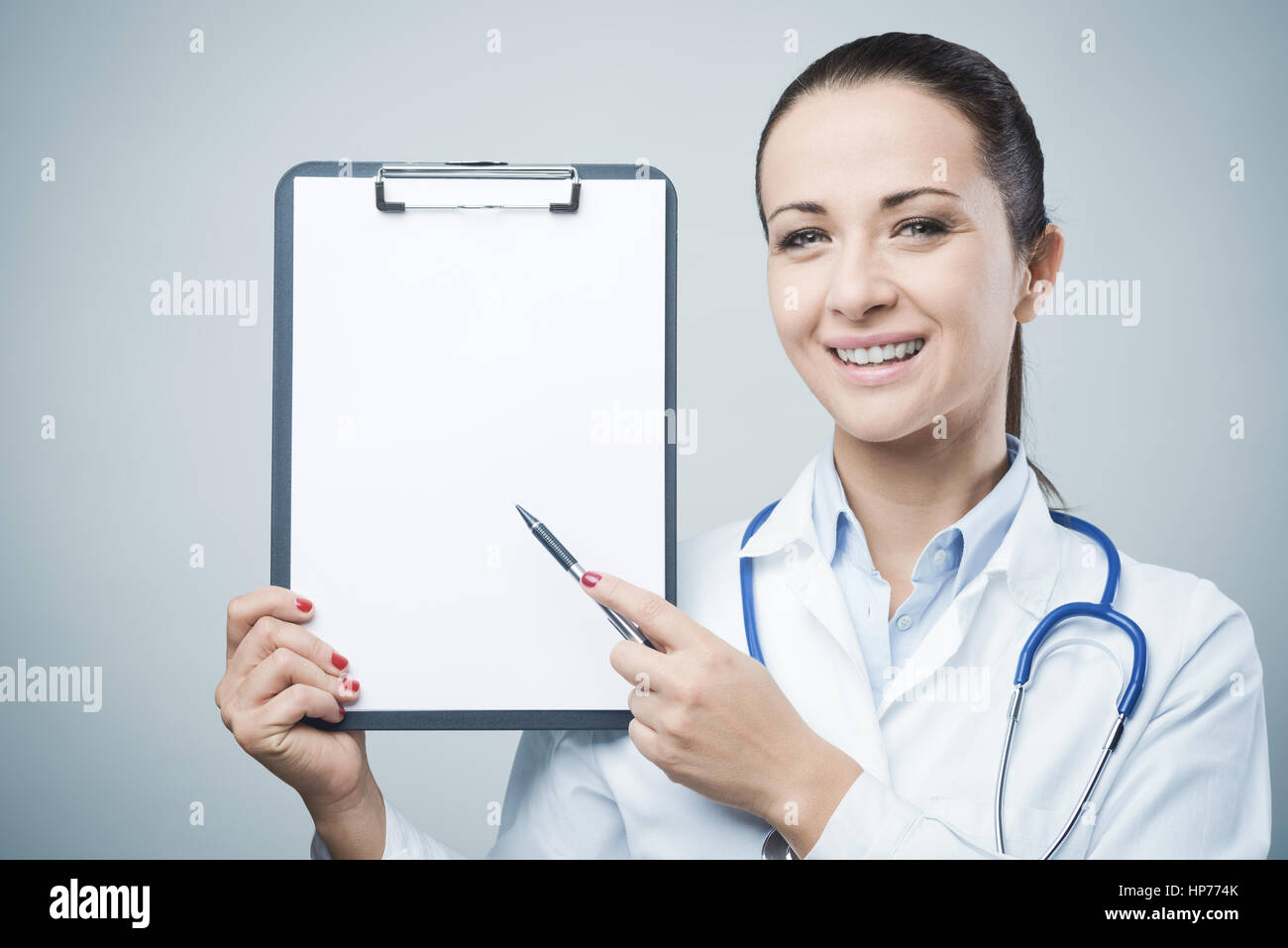 Female doctor smiling and showing a clipboard with an empty document ...