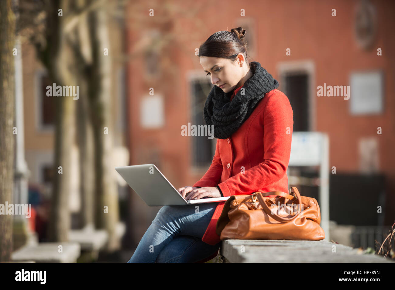 Smiling woman using her laptop in the street and connecting with a wi ...