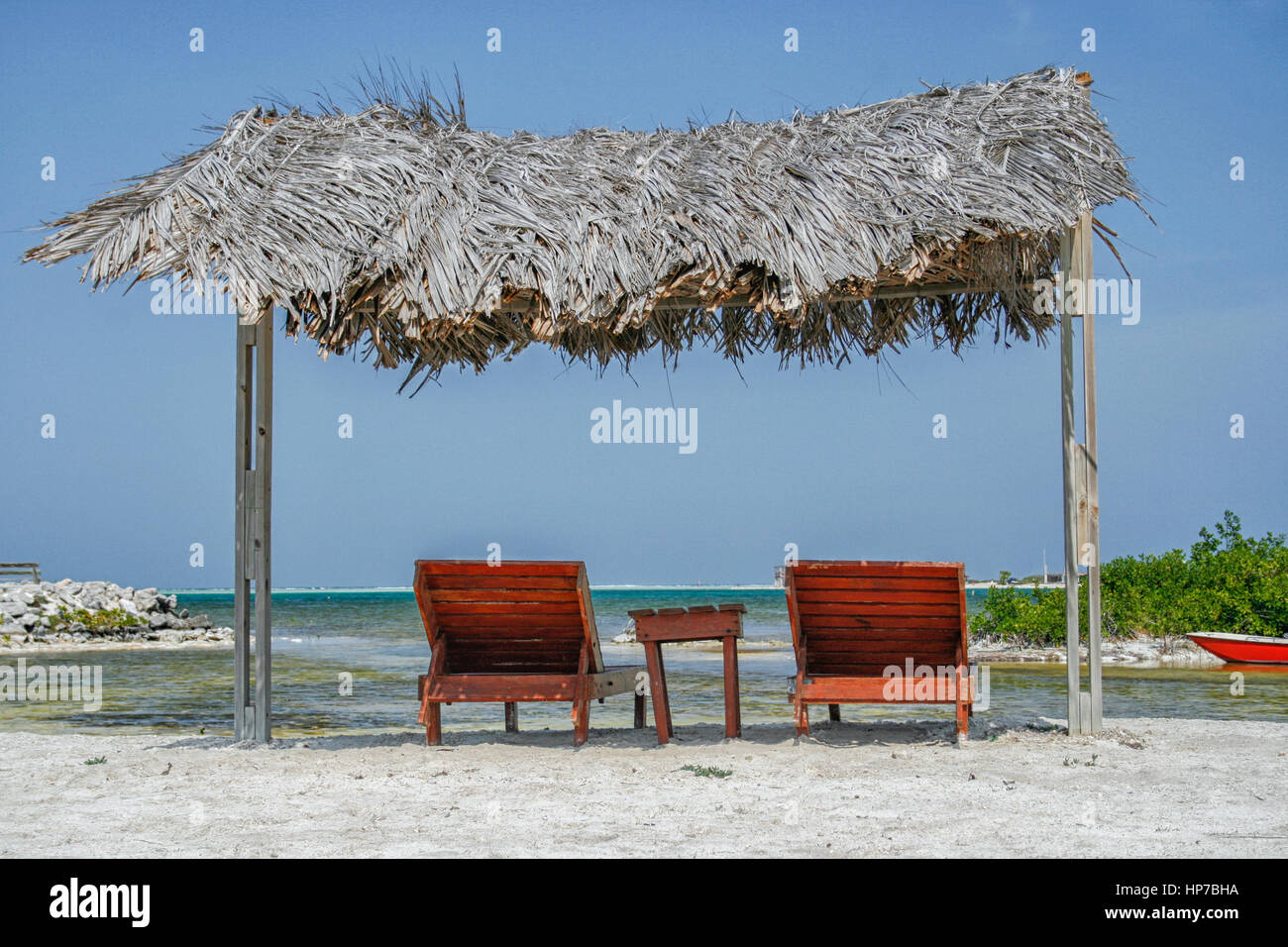Two wooden reclining chairs under a thatched roof on the beach in ...