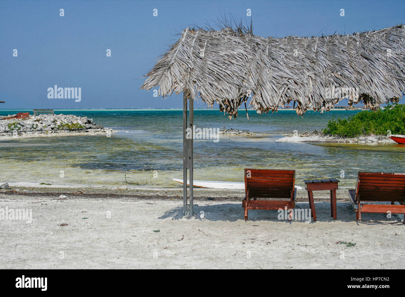 Two wooden reclining chairs under a thatched roof on a Caribbean beach ...