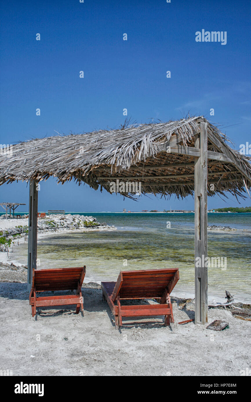 two wooden reclining chairs under a thatched roof on the beach in ...
