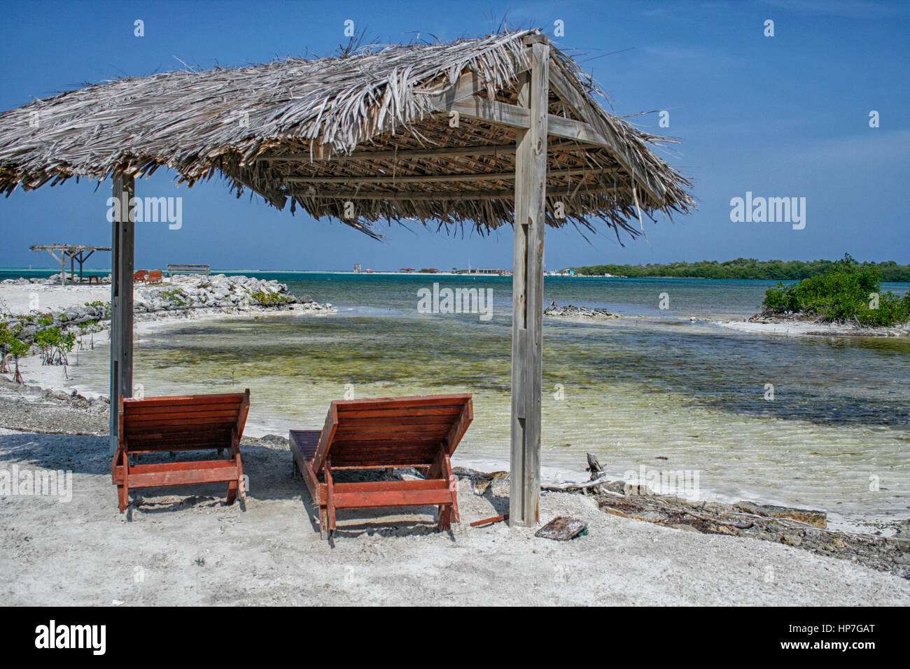 two wooden reclining chairs under a thatched roof on the beach in ...