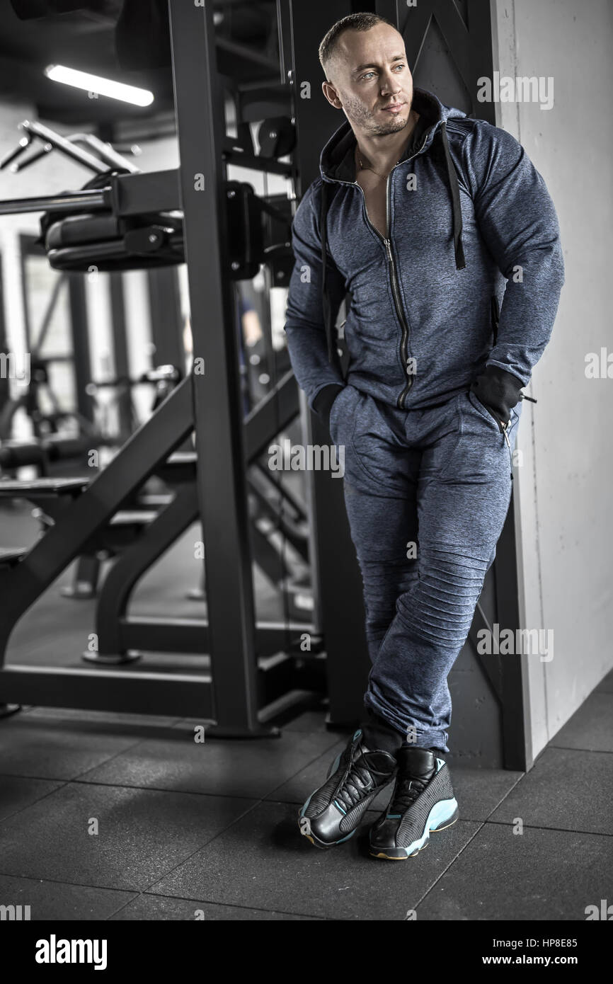 Mighty man with big muscles leans on the wall in the gym. He looks to ...