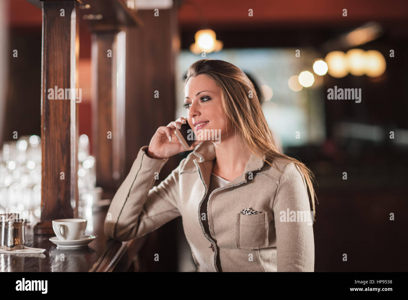 Smiling young woman at the bar having a phone call with her mobile ...