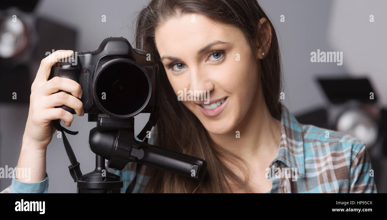 Young female photographer posing with a digital camera on tripod and ...