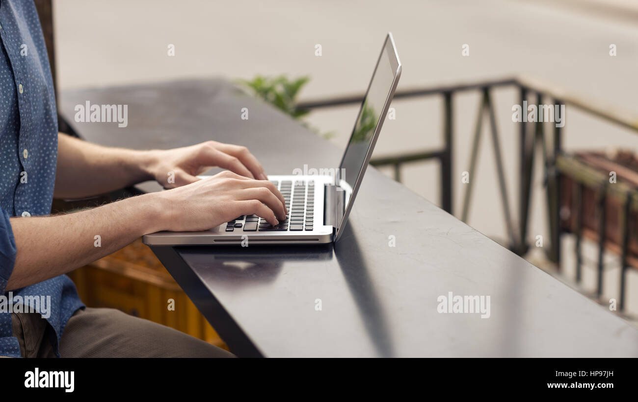 Unrecognizable man using a modern portable computer on an outdoor table ...