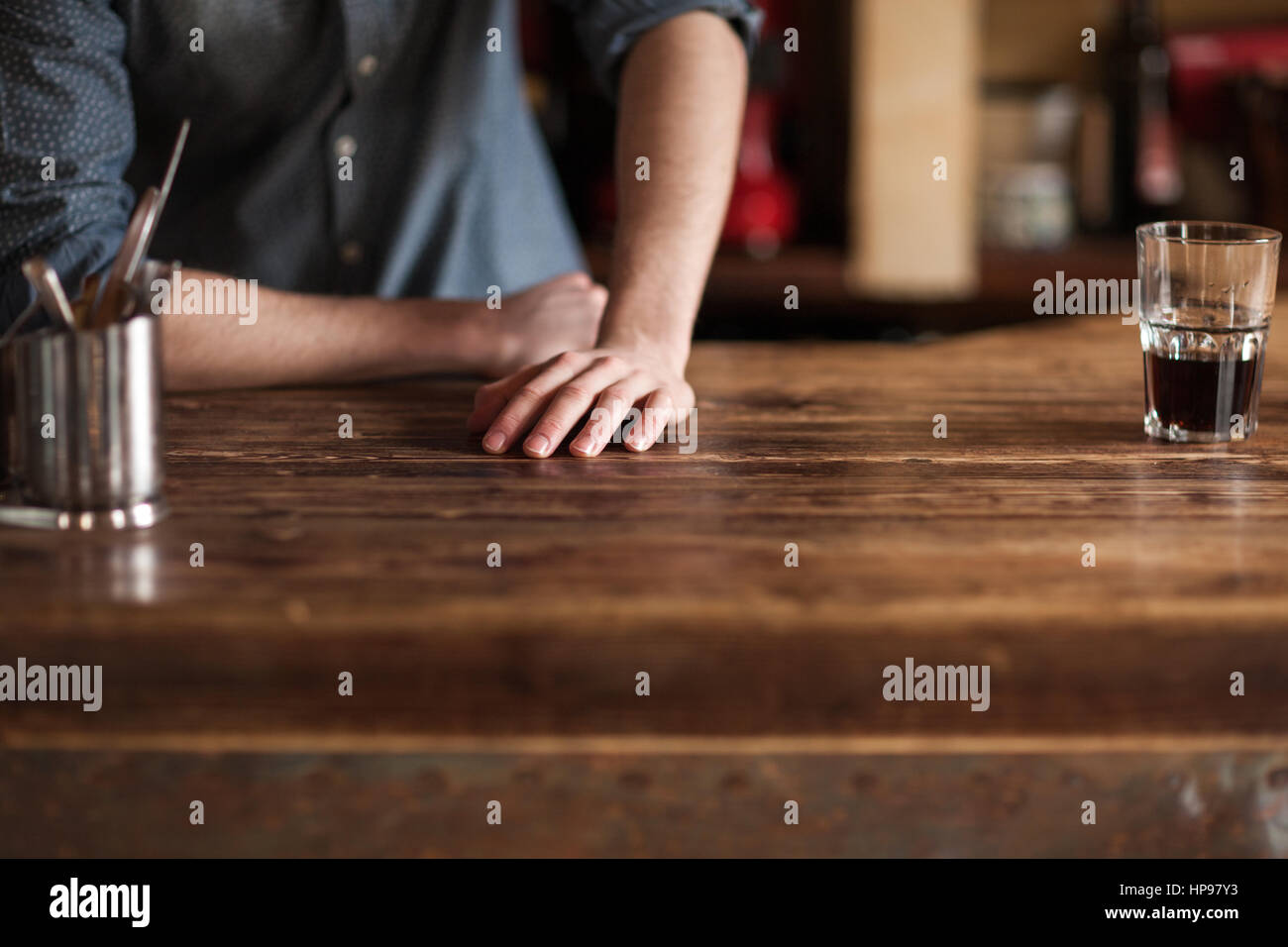 Young barman leaning on wooden bar counter hands close up ...