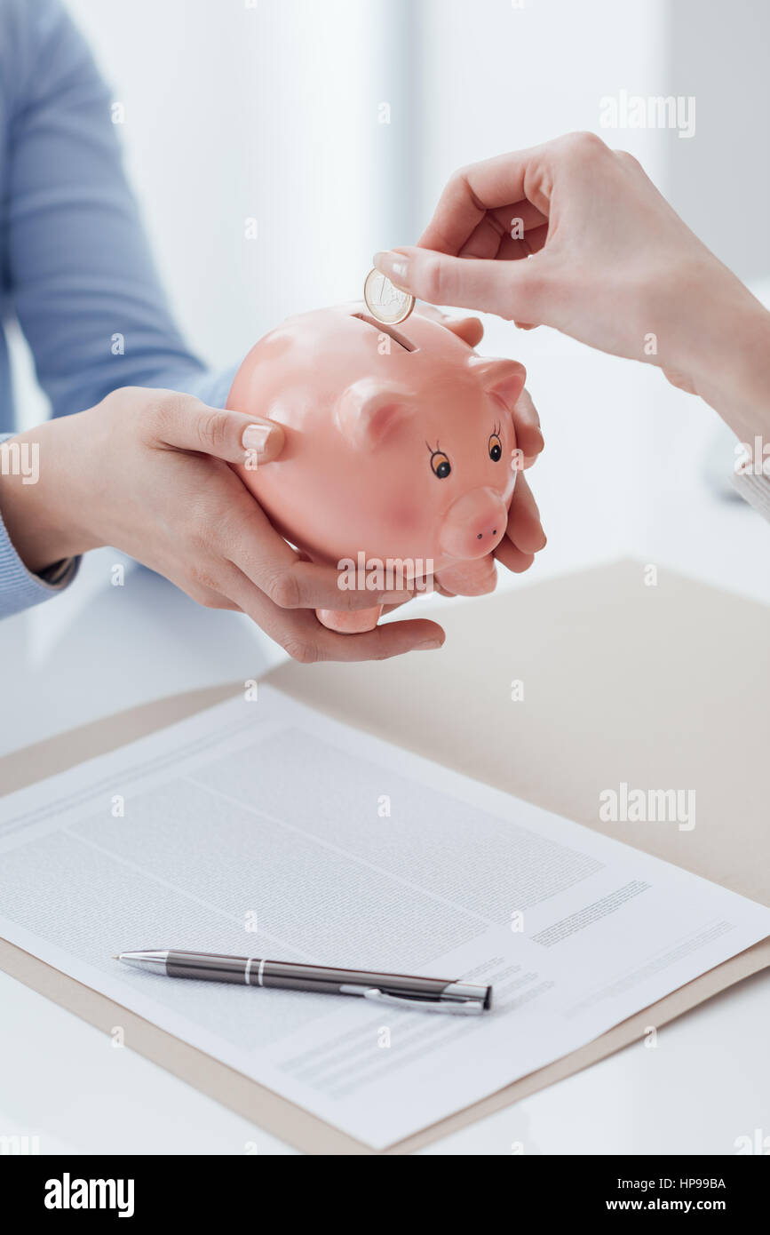 Financial advisor holding a piggy bank and customer inserting a coin ...