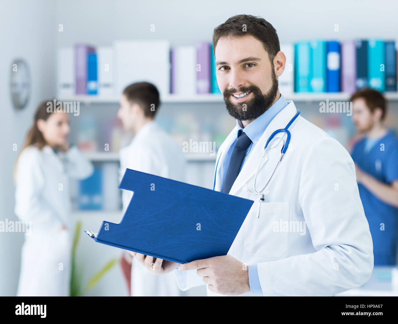 Confident young doctor posing in the office, he is smiling at camera ...