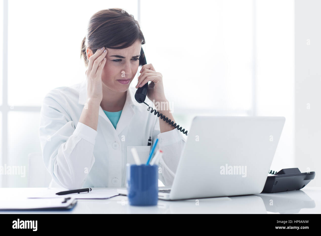 Stressed female doctor working at office desk and answering phone calls ...