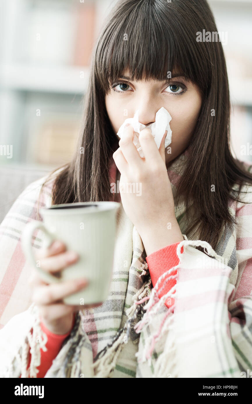 Sick woman at home having cold and flu, she is blowing her nose and ...