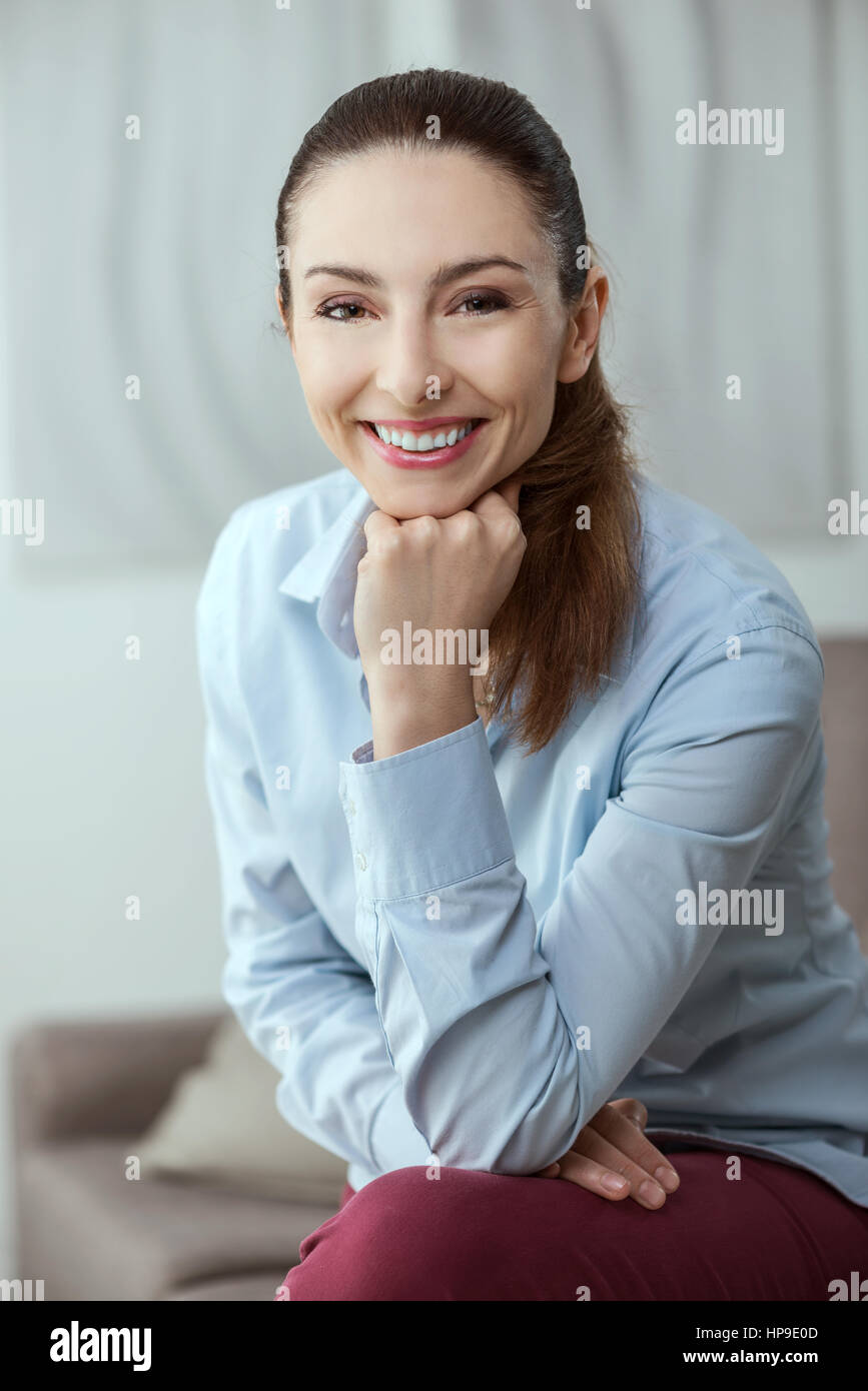 Attractive confident woman sitting on a couch, she is smiling at camera ...