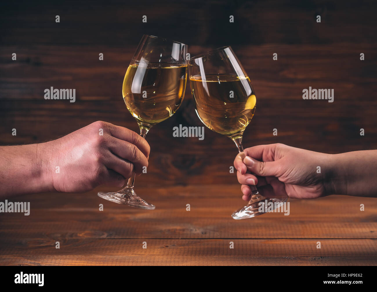 Hands of man and woman cheering with glasses of white wine against ...