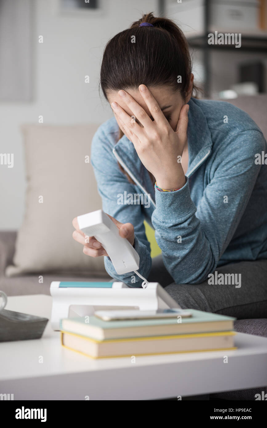 Sad depressed woman at home sitting on the sofa, she is calling an help ...