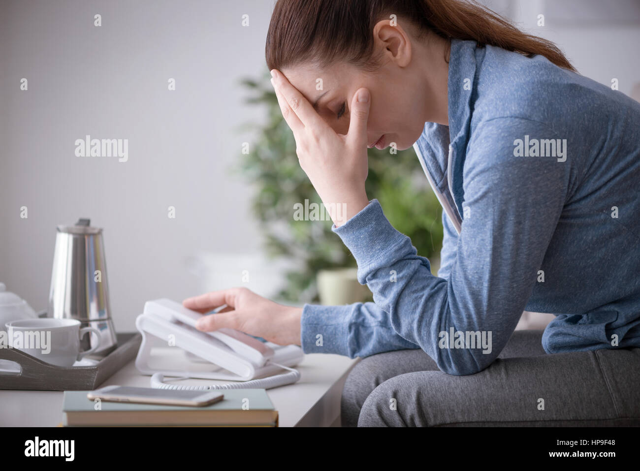 Sad depressed woman at home sitting on the sofa, she is calling an help ...