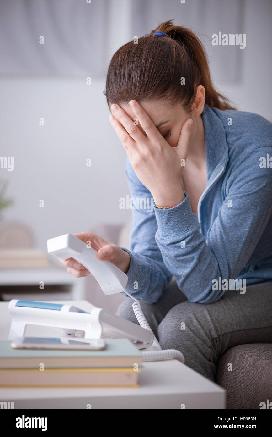 Sad depressed woman at home sitting on the sofa, she is calling an help ...