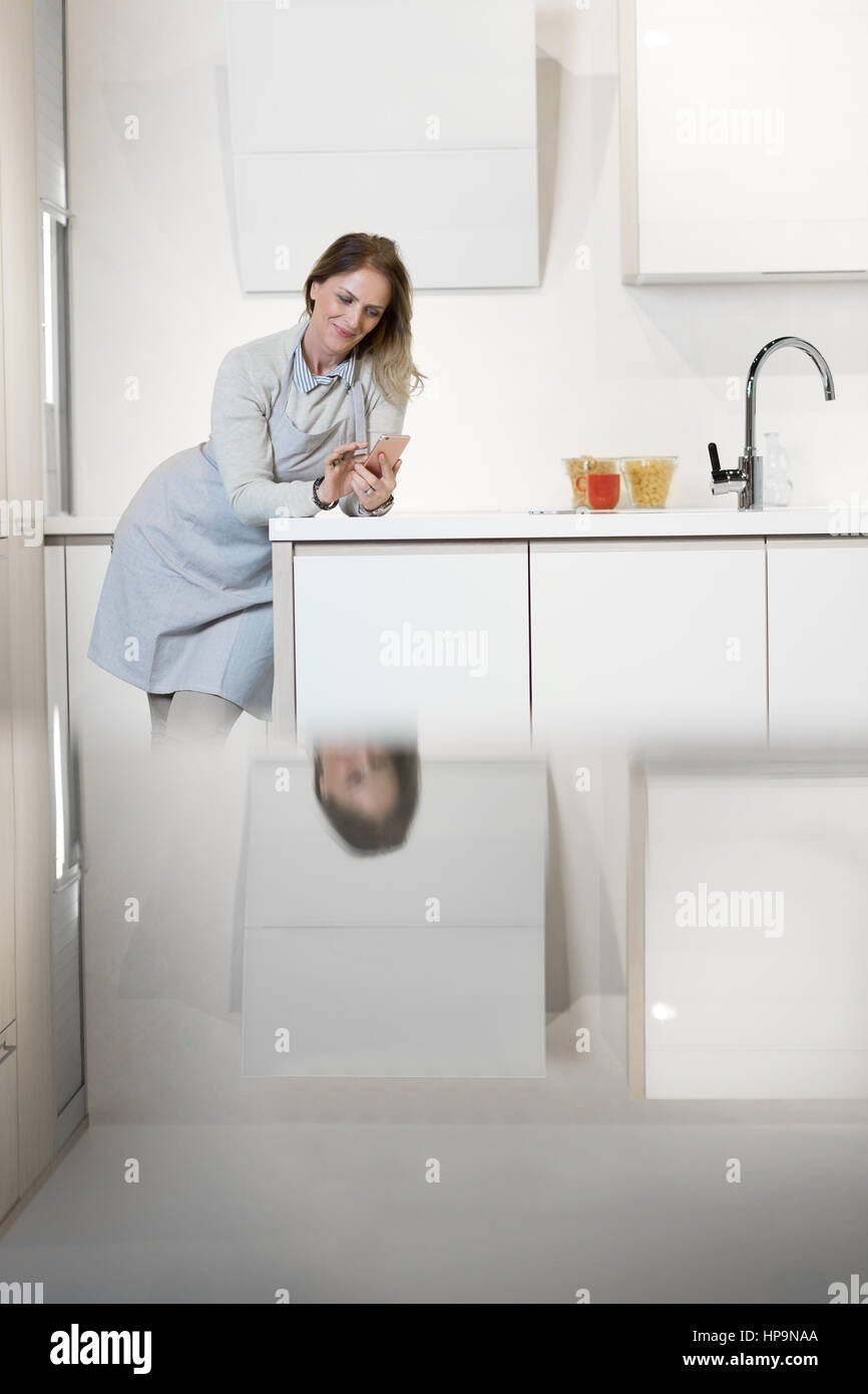 Woman texting on the phone in kitchen. Woman using technology in ...