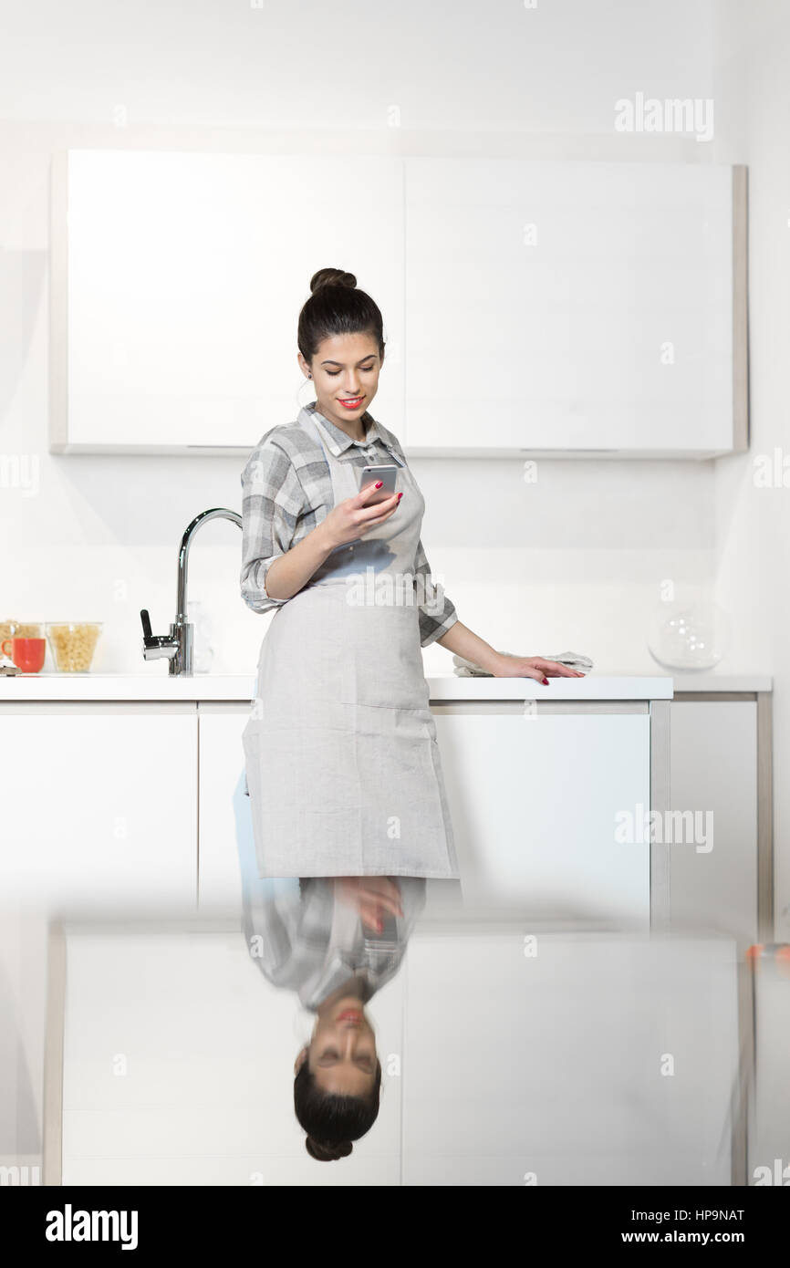 Woman texting on the phone in kitchen. Woman using technology in ...